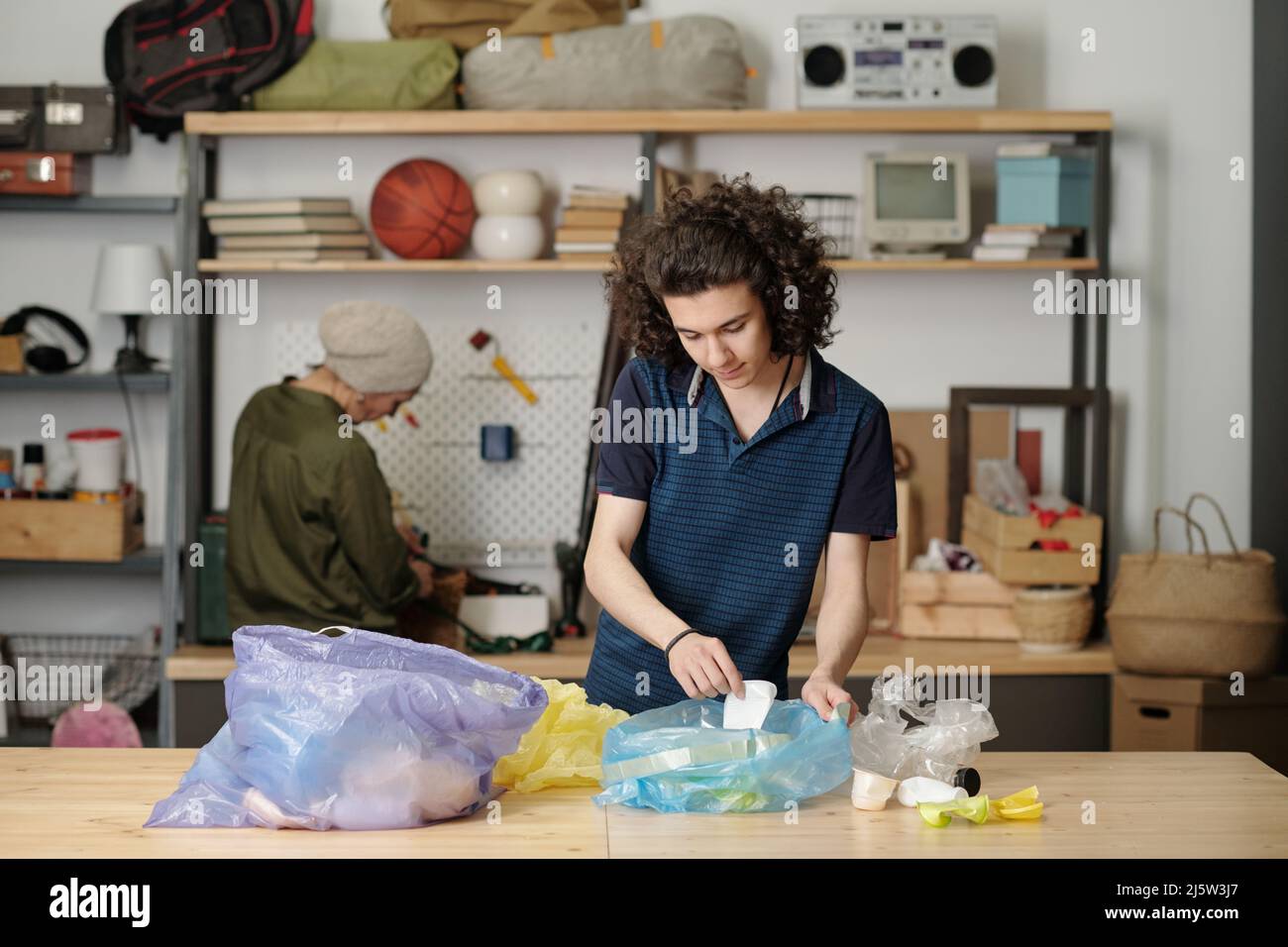 Teenage guy sorting waste and putting it into two large cellophane ...