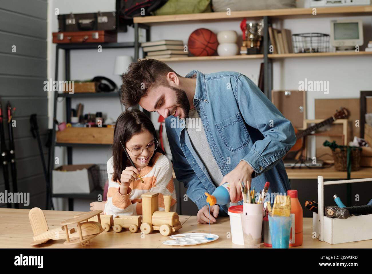 Young creative man with plastic bottle pouring blue liquid paint on ...
