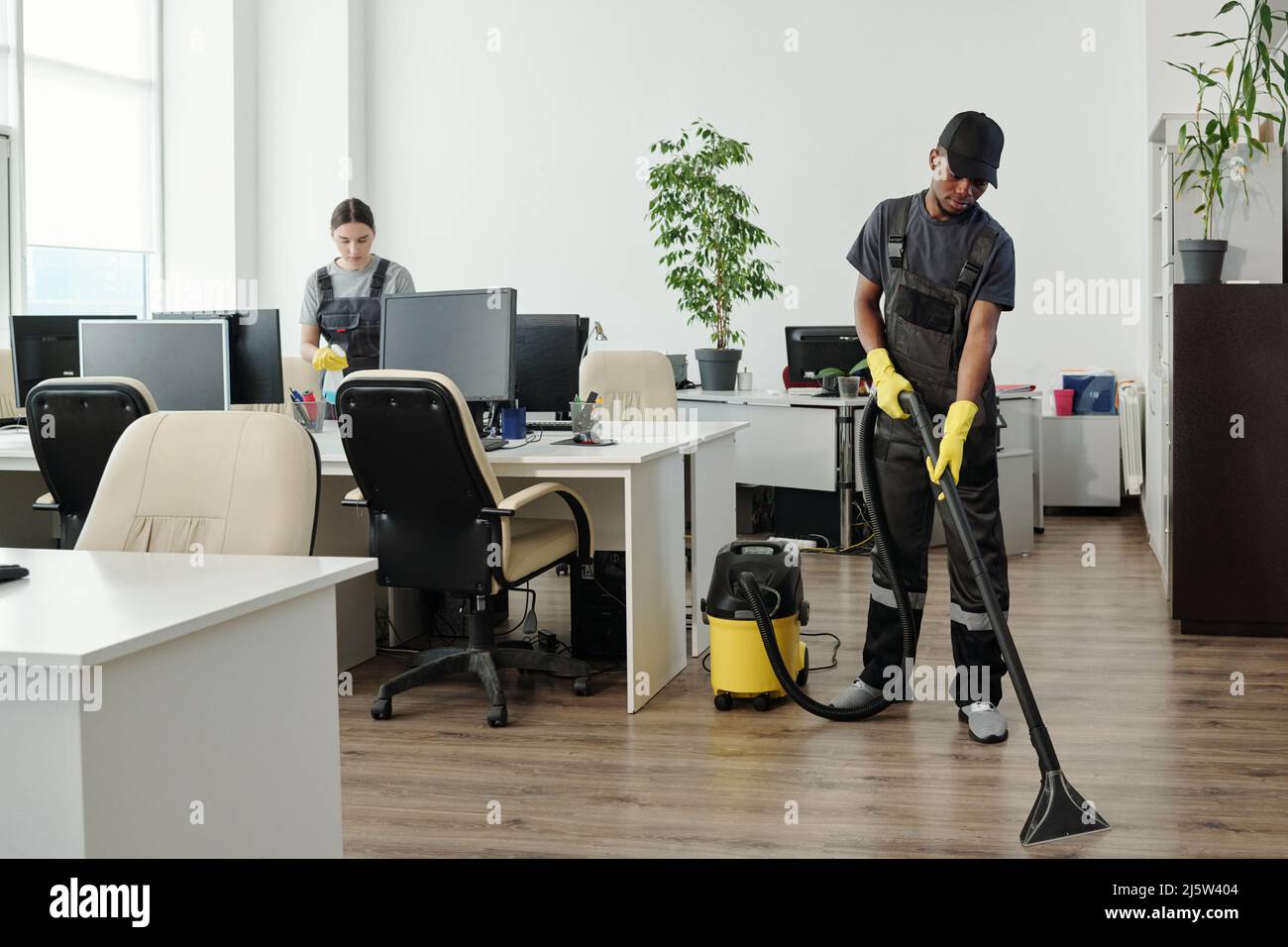 Young African American man in workwear cleaning floor of contemporary ...
