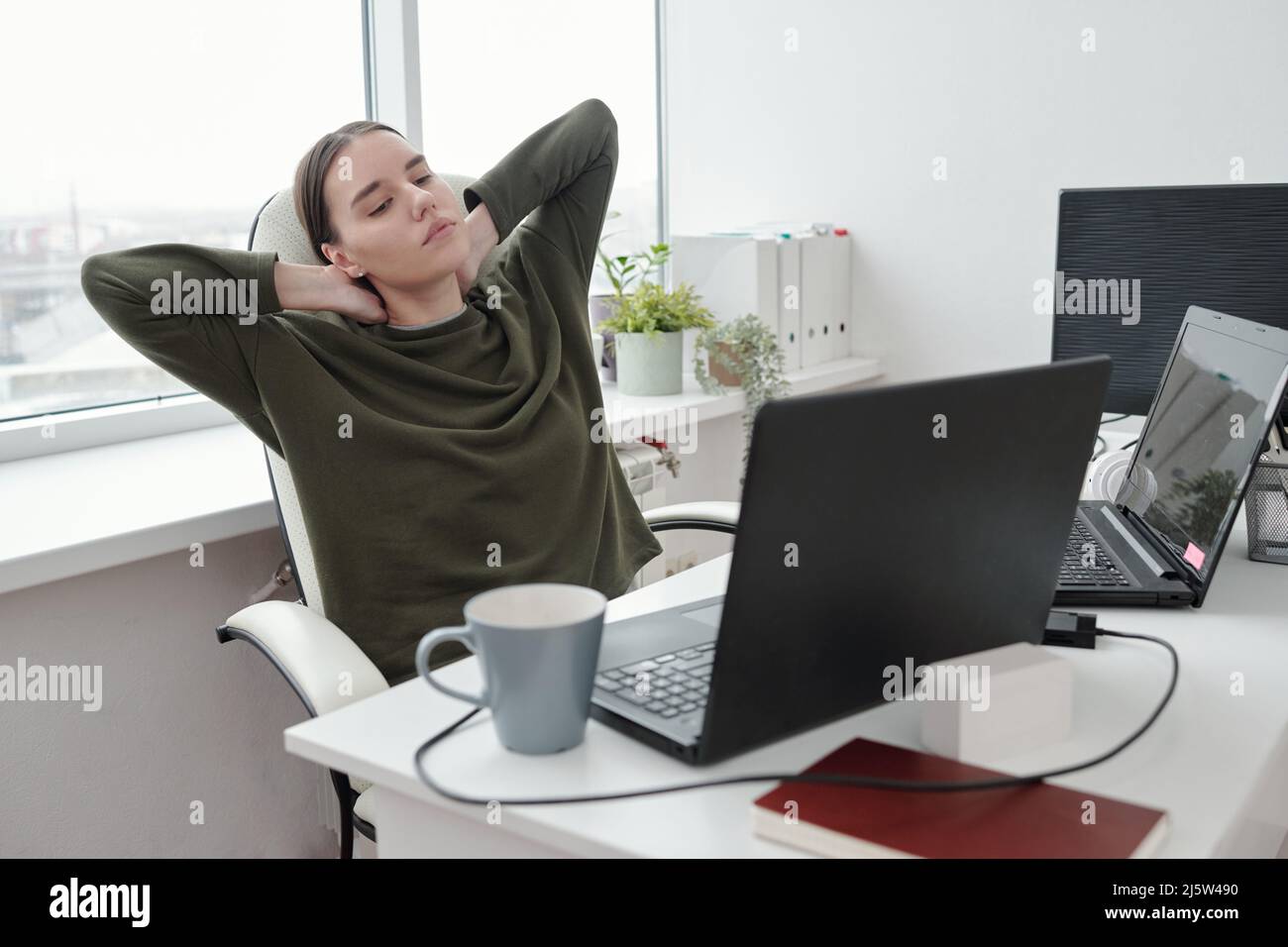 Young relaxed female programmer doing exercise for neck and arms while ...
