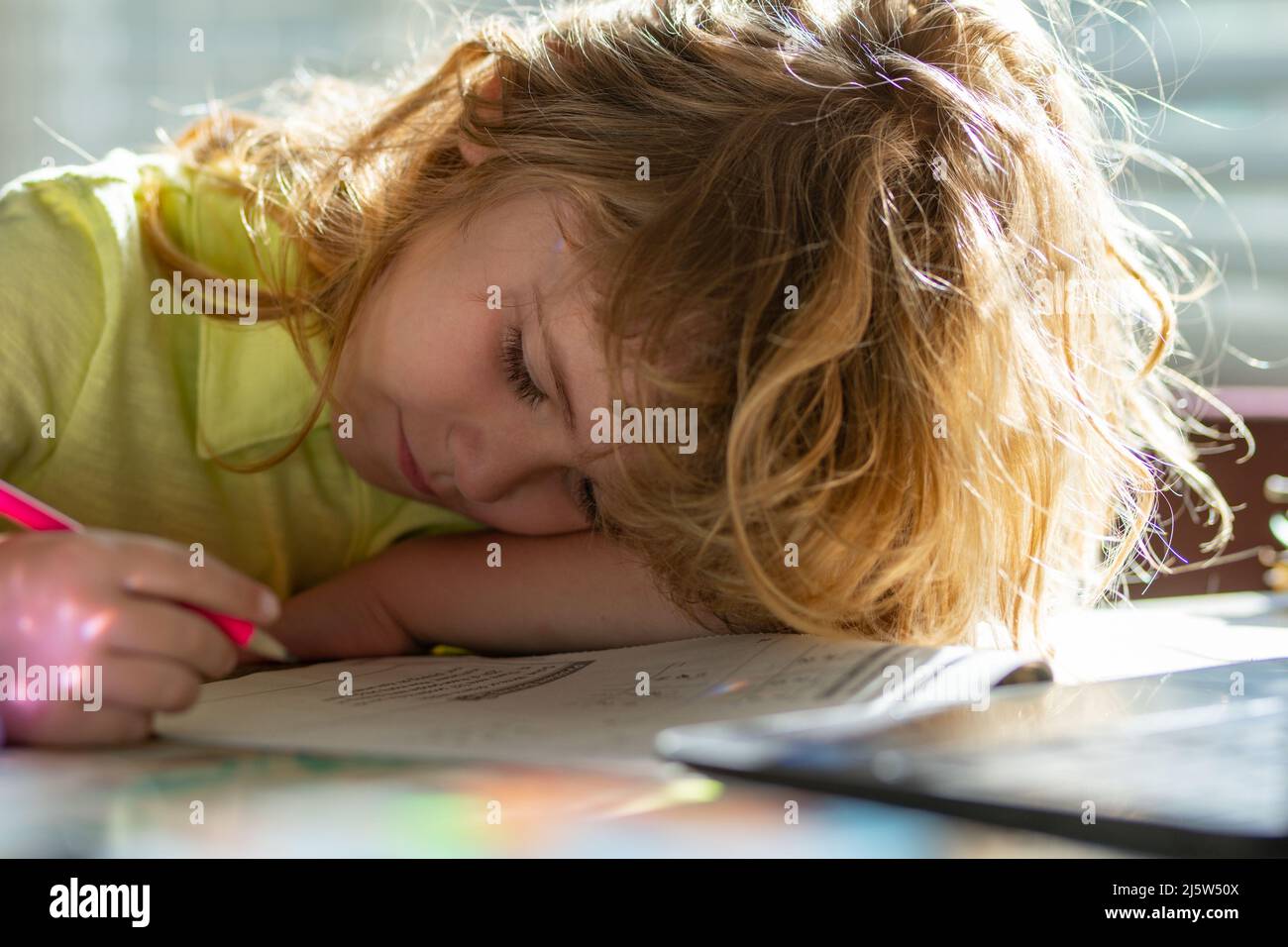 Tired schoolboy while doing homework. Cute boy doing homework, writing ...