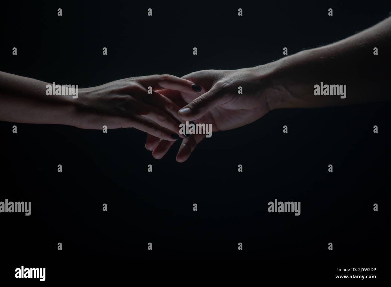 Two hands stretch each other, black background. Couple in love holding ...