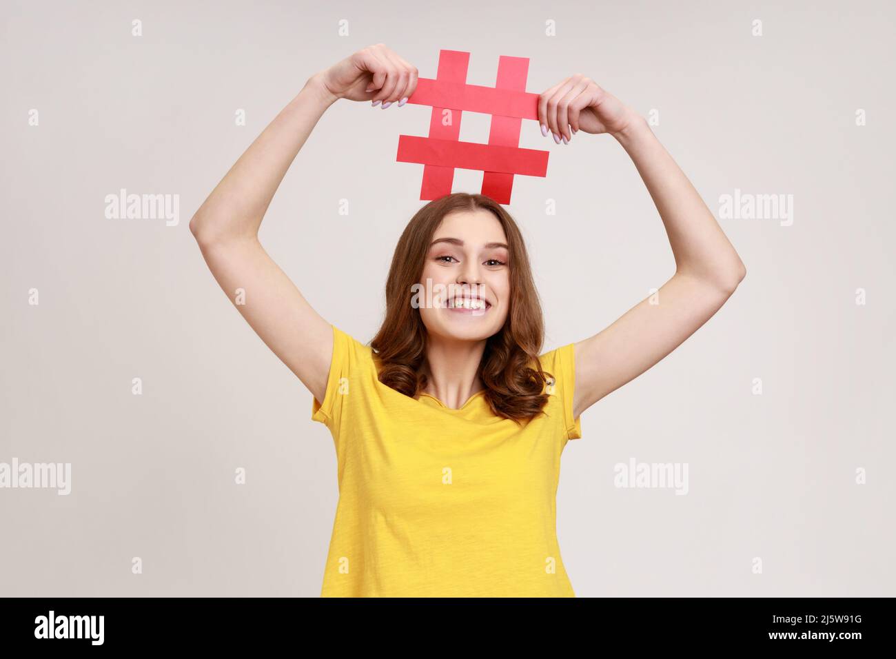 Happy teen girl with toothy smile in yellow t-shirt holding red hashtag ...