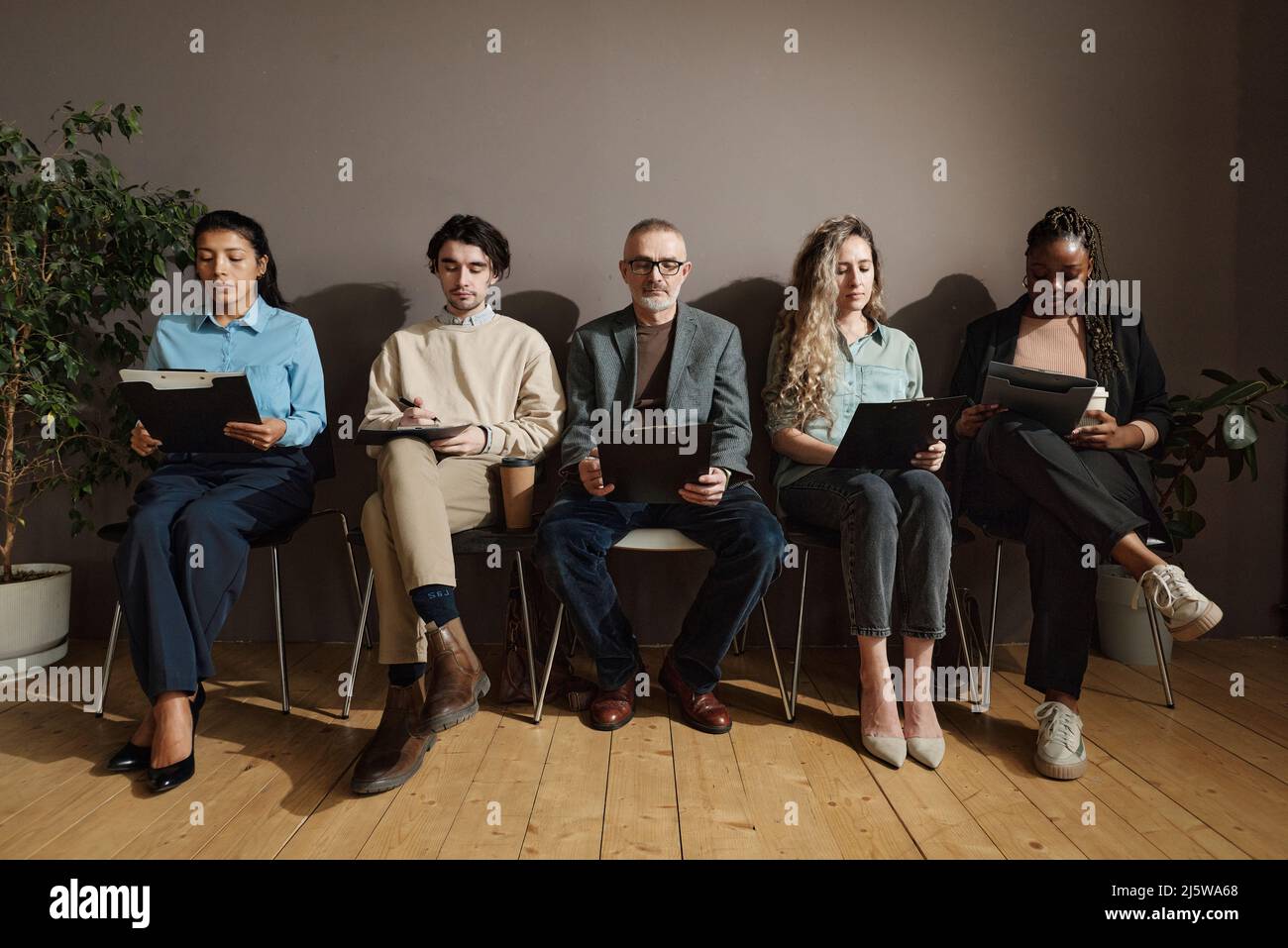 Group of business people sitting on chairs in waiting room and reading ...