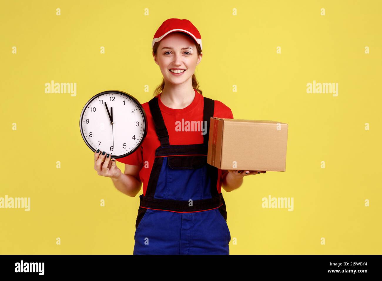 Portrait of delighted courier woman standing with cardboard parcel and ...