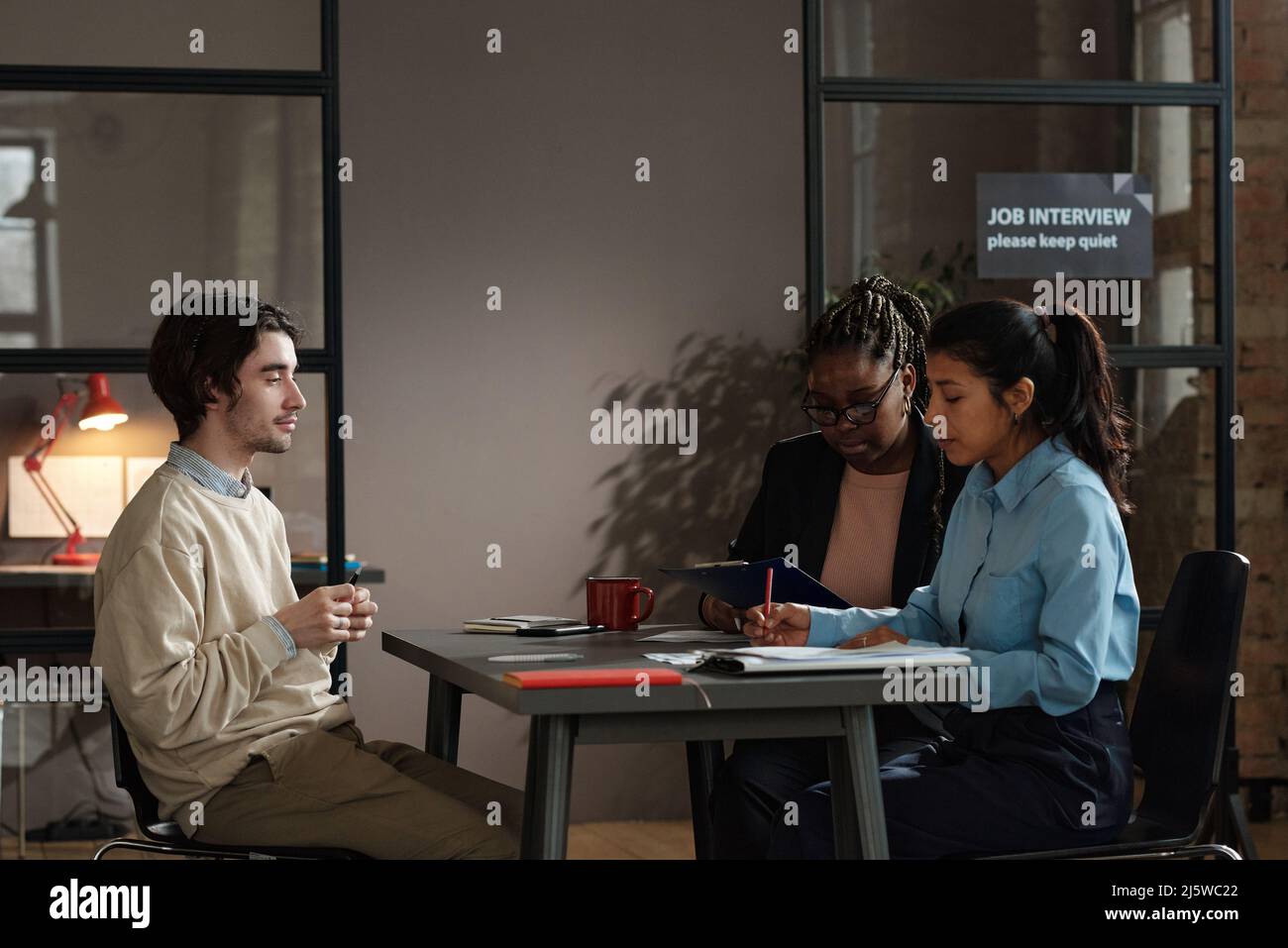 Manager examining resume of young man with her colleague at table ...