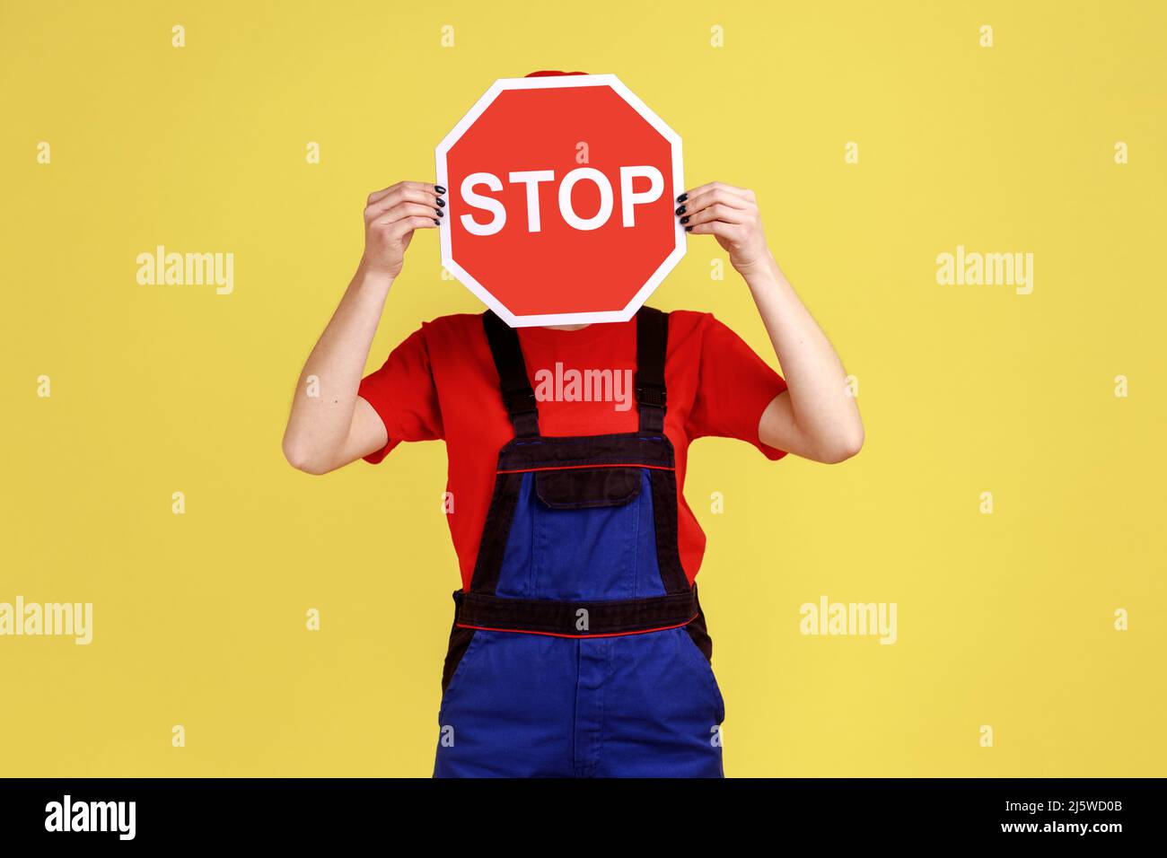 Portrait of worker woman standing hiding her face behind red stop sign ...