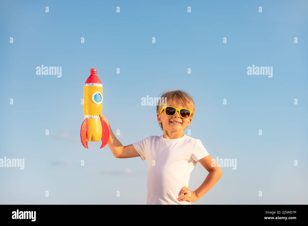 Happy child playing outdoor with toy rocket against blue summer sky ...