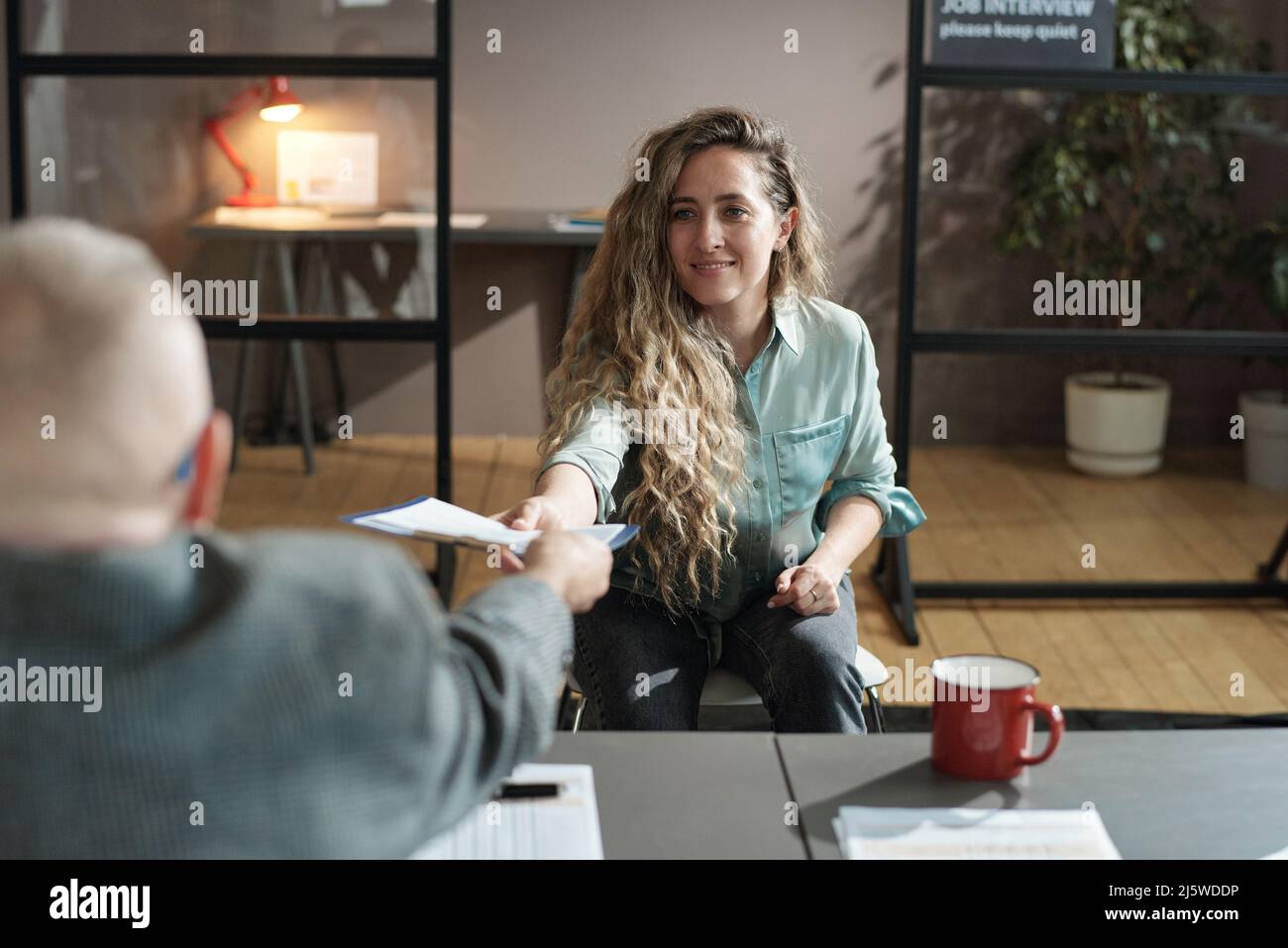 Young smiling woman giving her resume to interviewer during interview ...