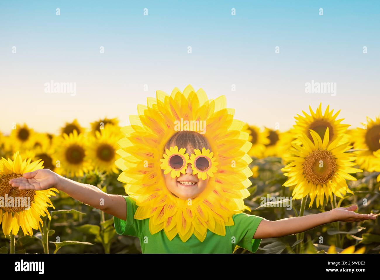 Happy child having fun in spring field of sunflowers. Outdoor portrait ...