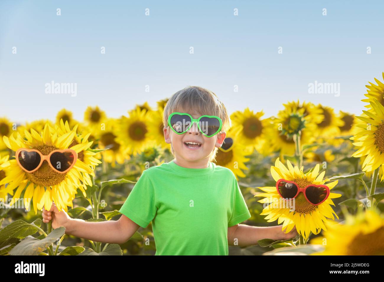 Happy child having fun in spring field of sunflowers. Outdoor portrait ...