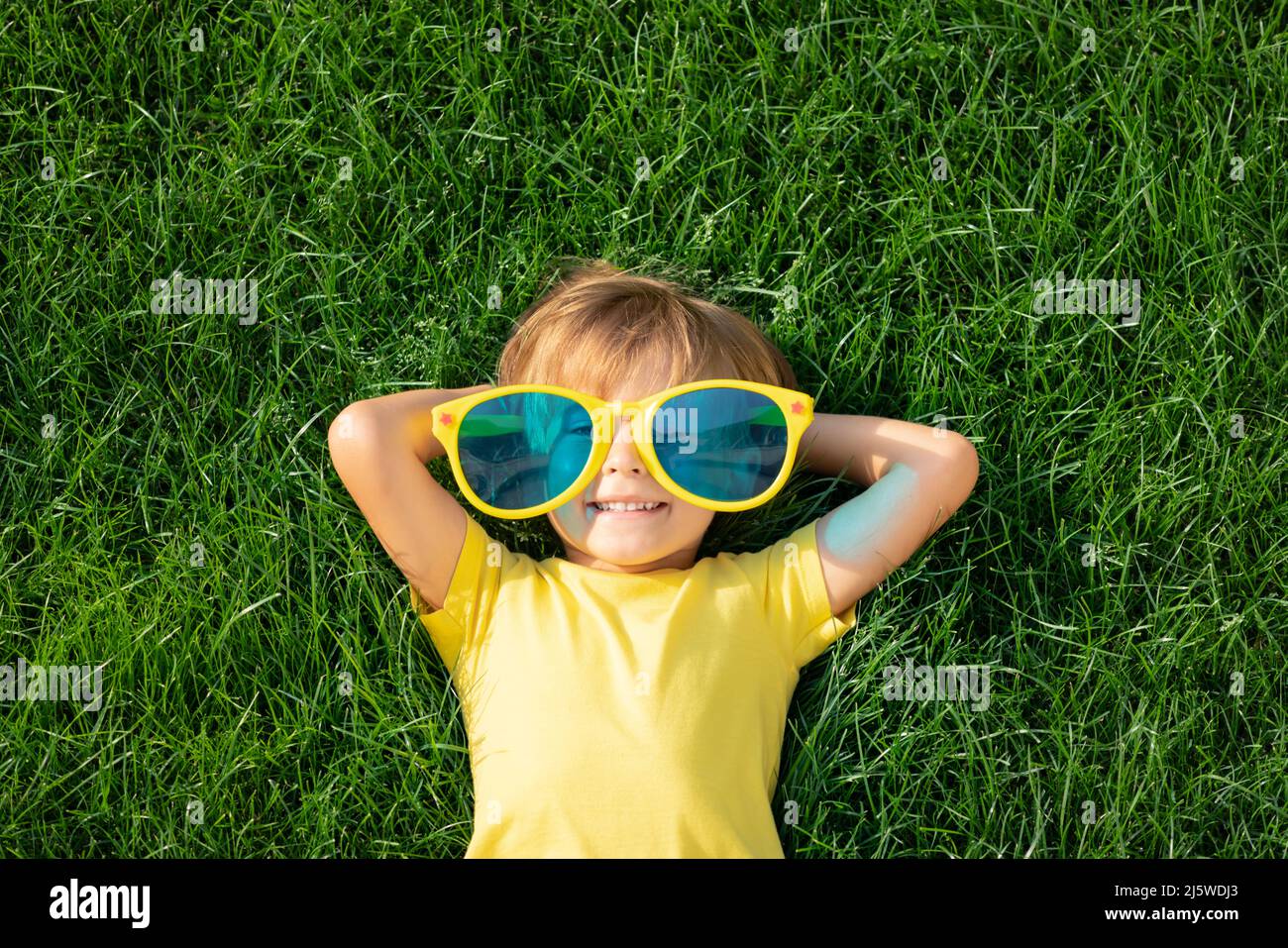 Happy child playing outdoor in spring park. Kid lying on green grass ...