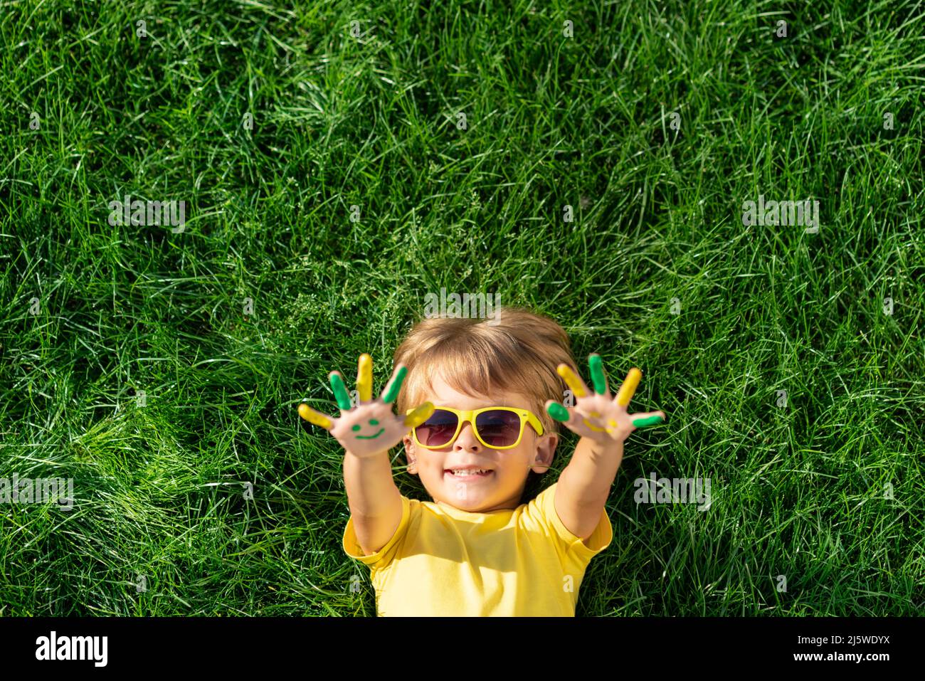 Happy child with smile on hands outdoor. Kid on green spring grass ...