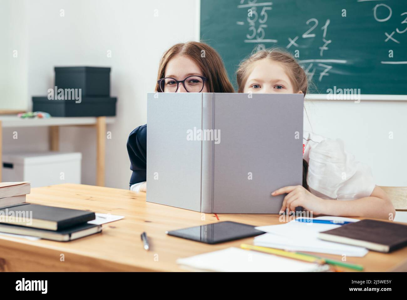 Schoolgirls hiding behind book sitting in a classroom Stock Photo - Alamy
