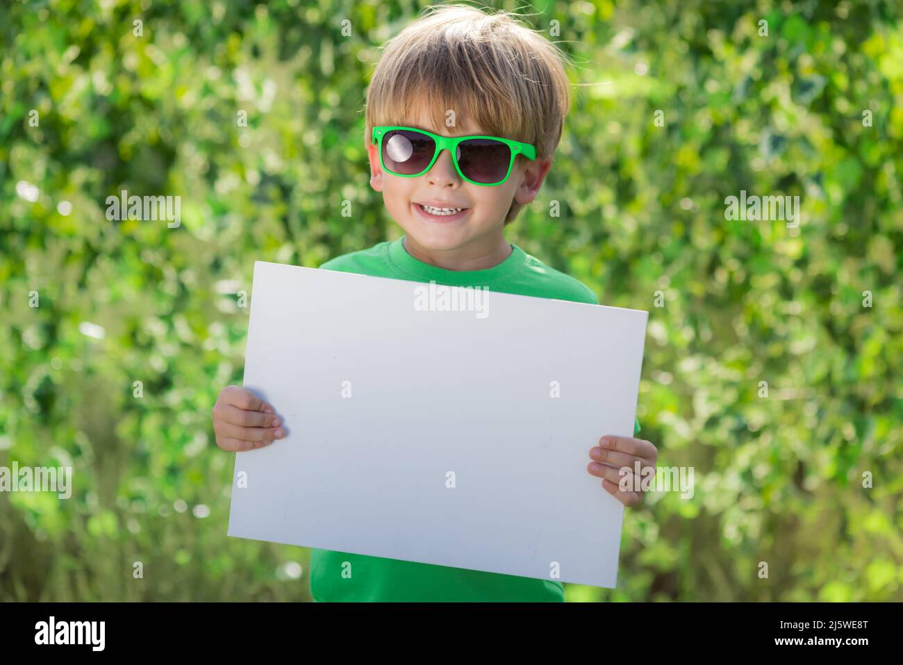 Happy child showing paper blank. Portrait of kid outdoor. Boy against ...