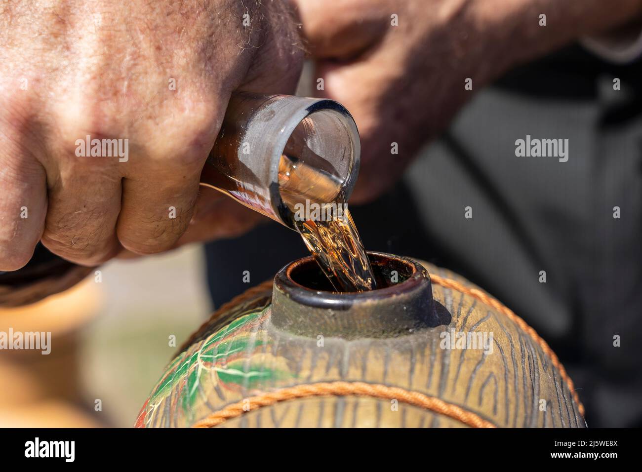 Man pouring wine from the glass bottle into a ceramic barrel. Hand and ...