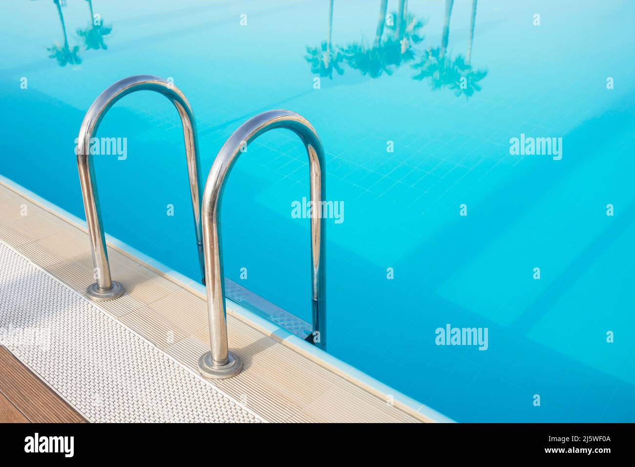 Palm trees are reflected in a pool of turquoise water. Metal ladder for ...