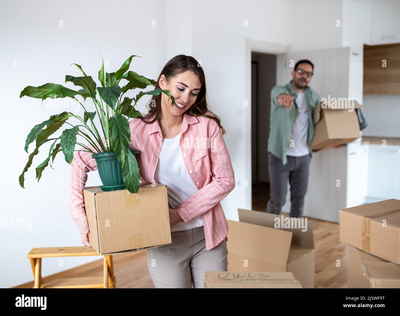 Couple Moving In In Their New Apartment Carrying Cardboard Boxes While