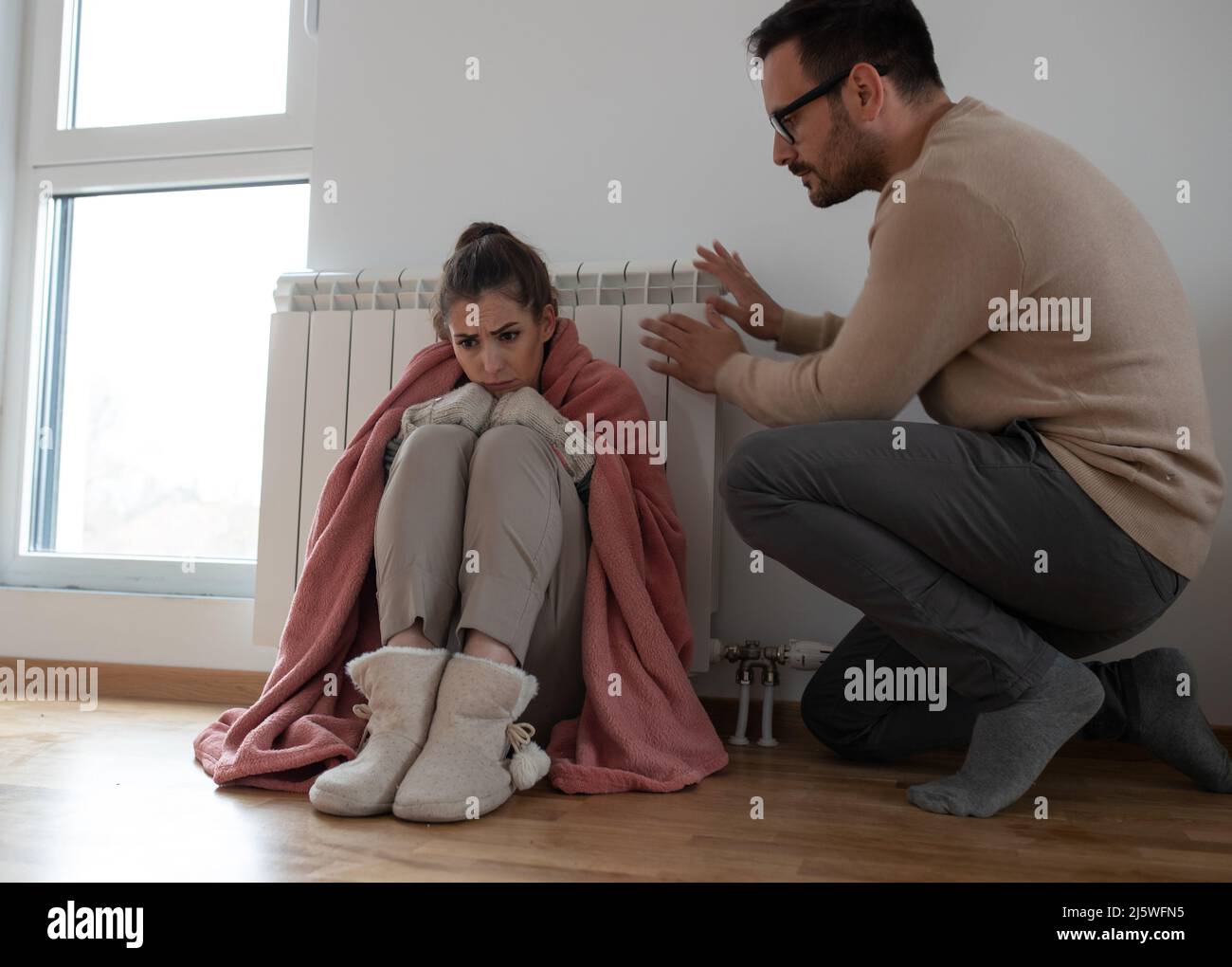 Woman sitting on the floor covered with blanket feeling cold while man ...