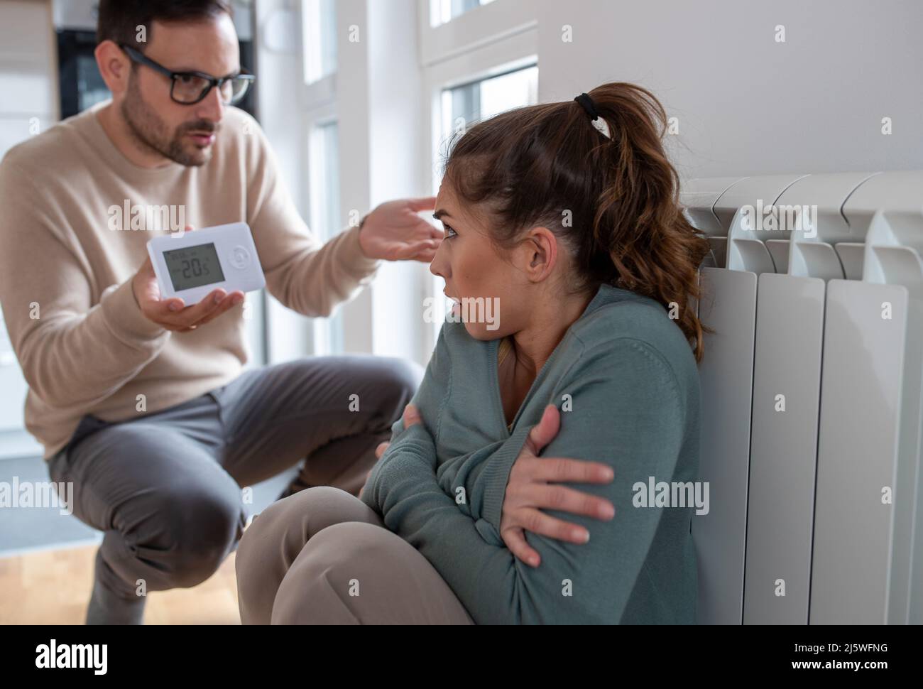 Woman sits on the floor next to radiator trying to warm up while man ...