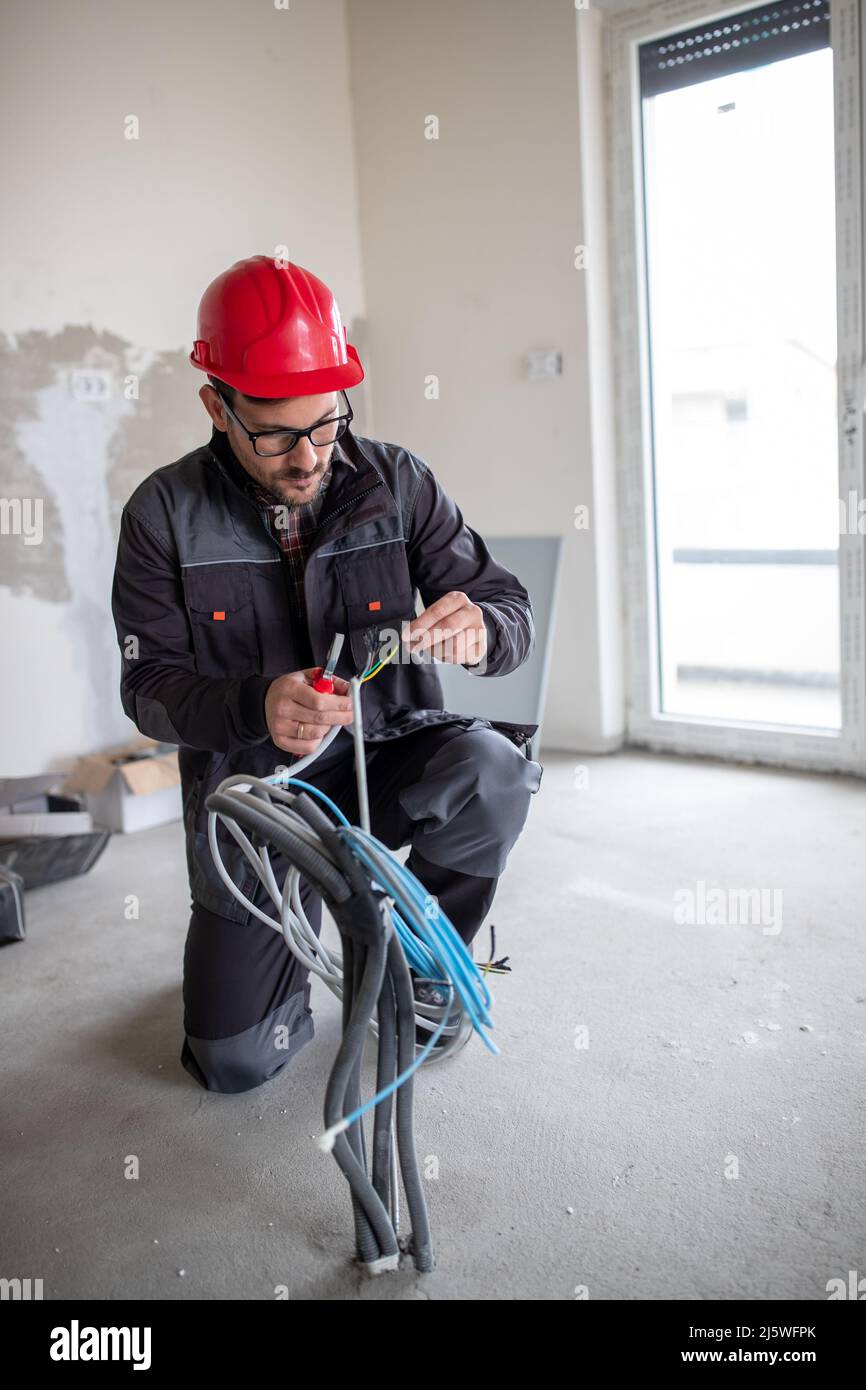 Male electrician in uniform with helmet using pliers to cut electrical ...