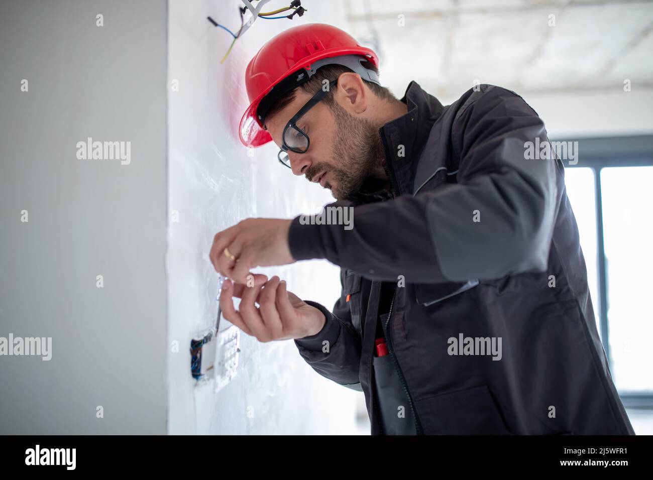 Serious male electrician with helmet installing power socket in the ...