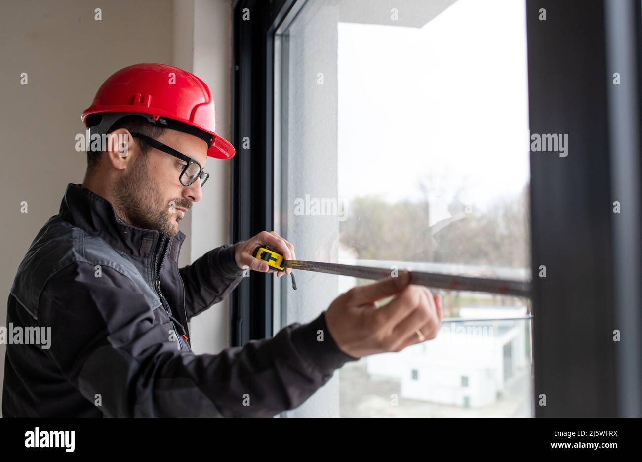 Male worker wearing helmet measuring window with measuring tape for ...
