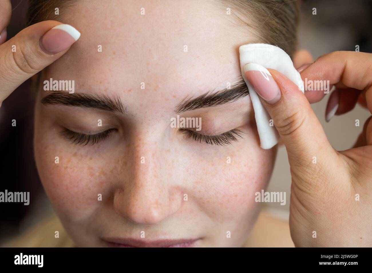 The master processes the eyebrows of a Caucasian woman with a cotton ...