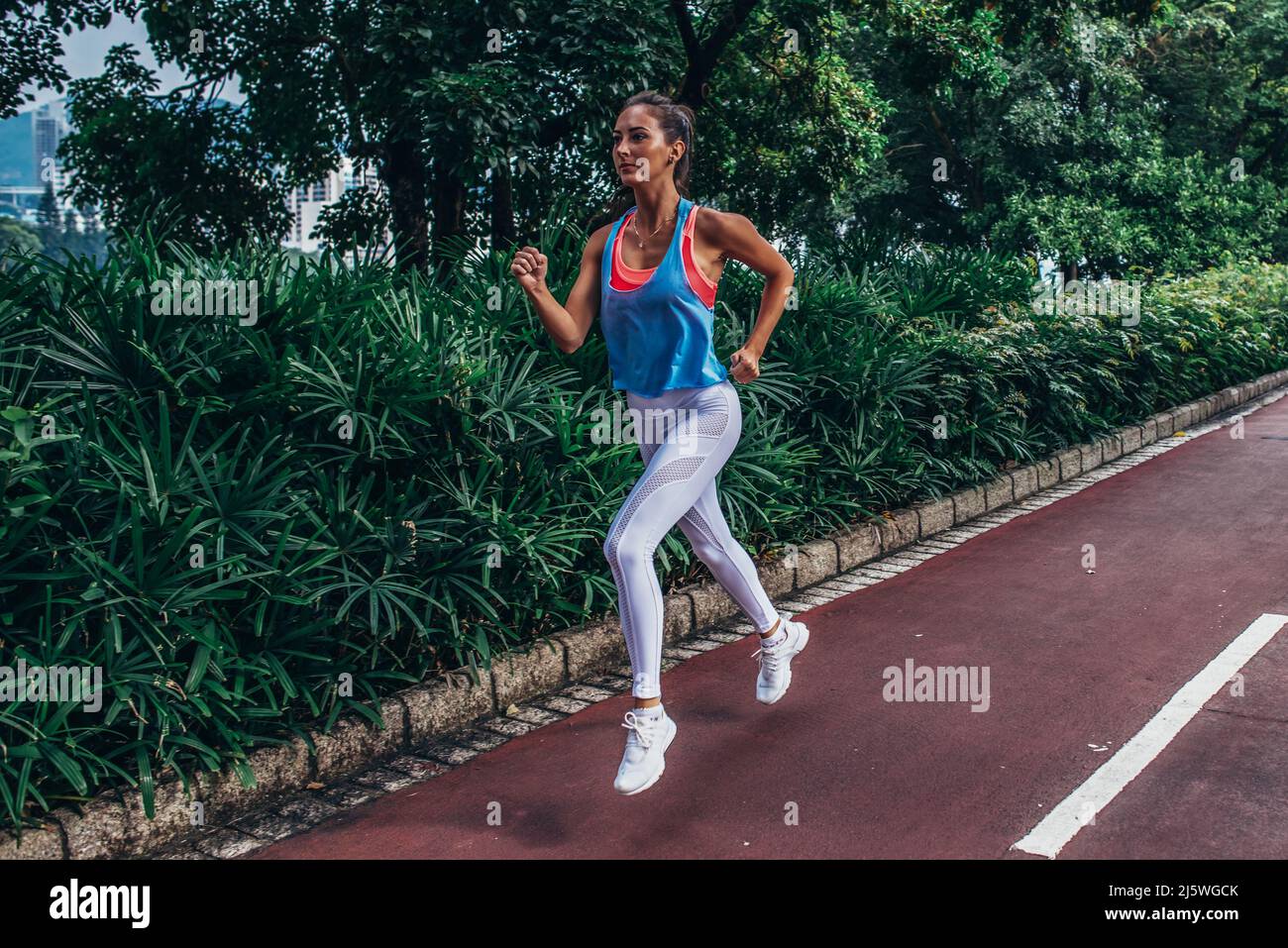Fit young woman jogging down lane with trees on sides in the park in ...
