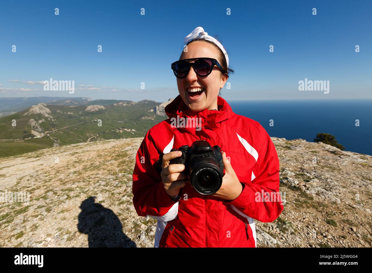 Happy woman photographer smiles on a peak of a mountain with dslr ...
