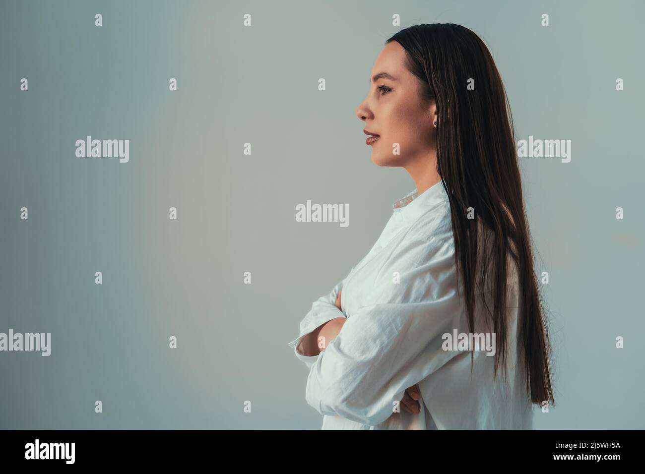 Young confident brunette woman in white shirt looks forward with arms ...