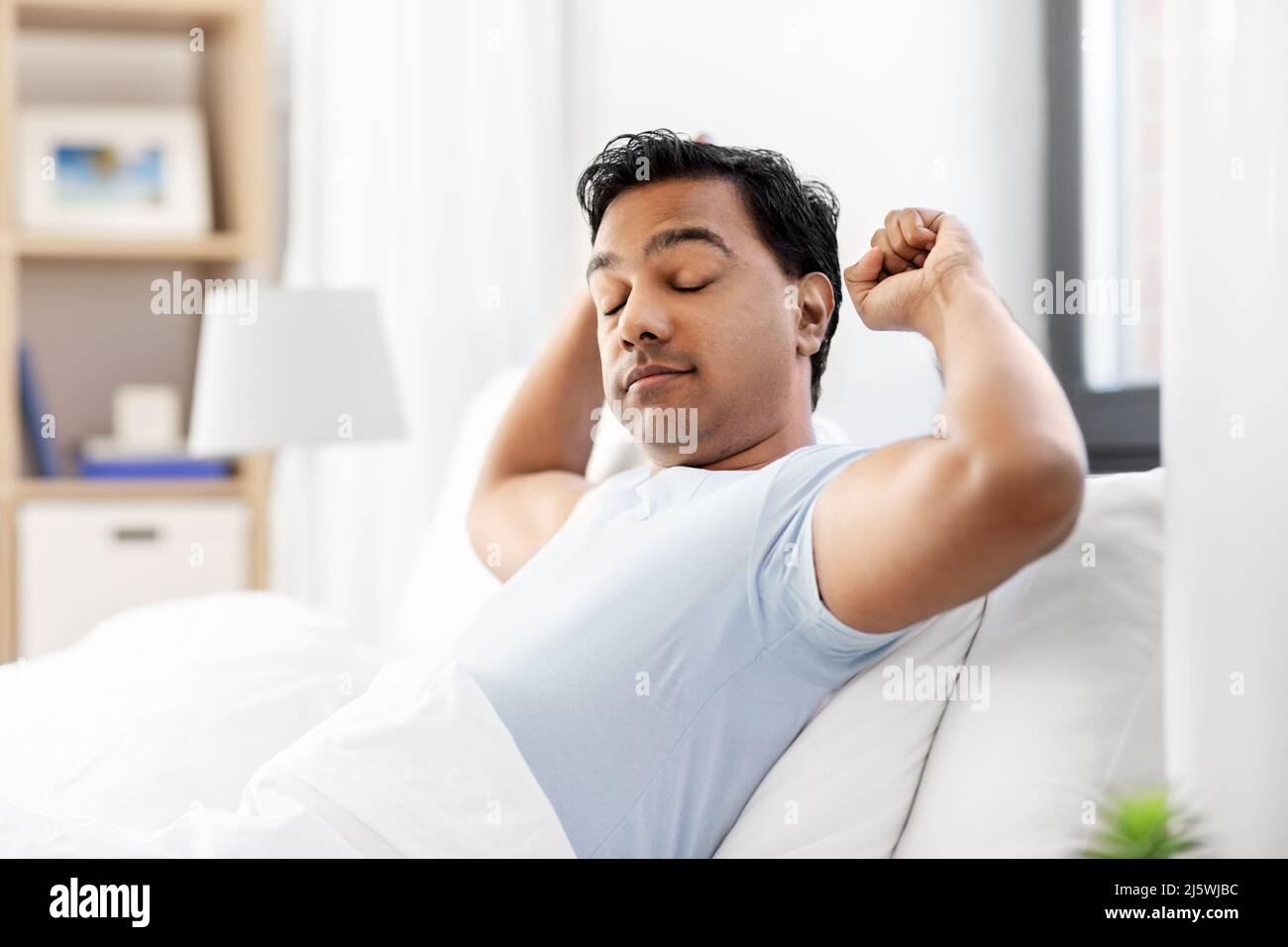 sleepy indian man stretching in bed at home Stock Photo - Alamy