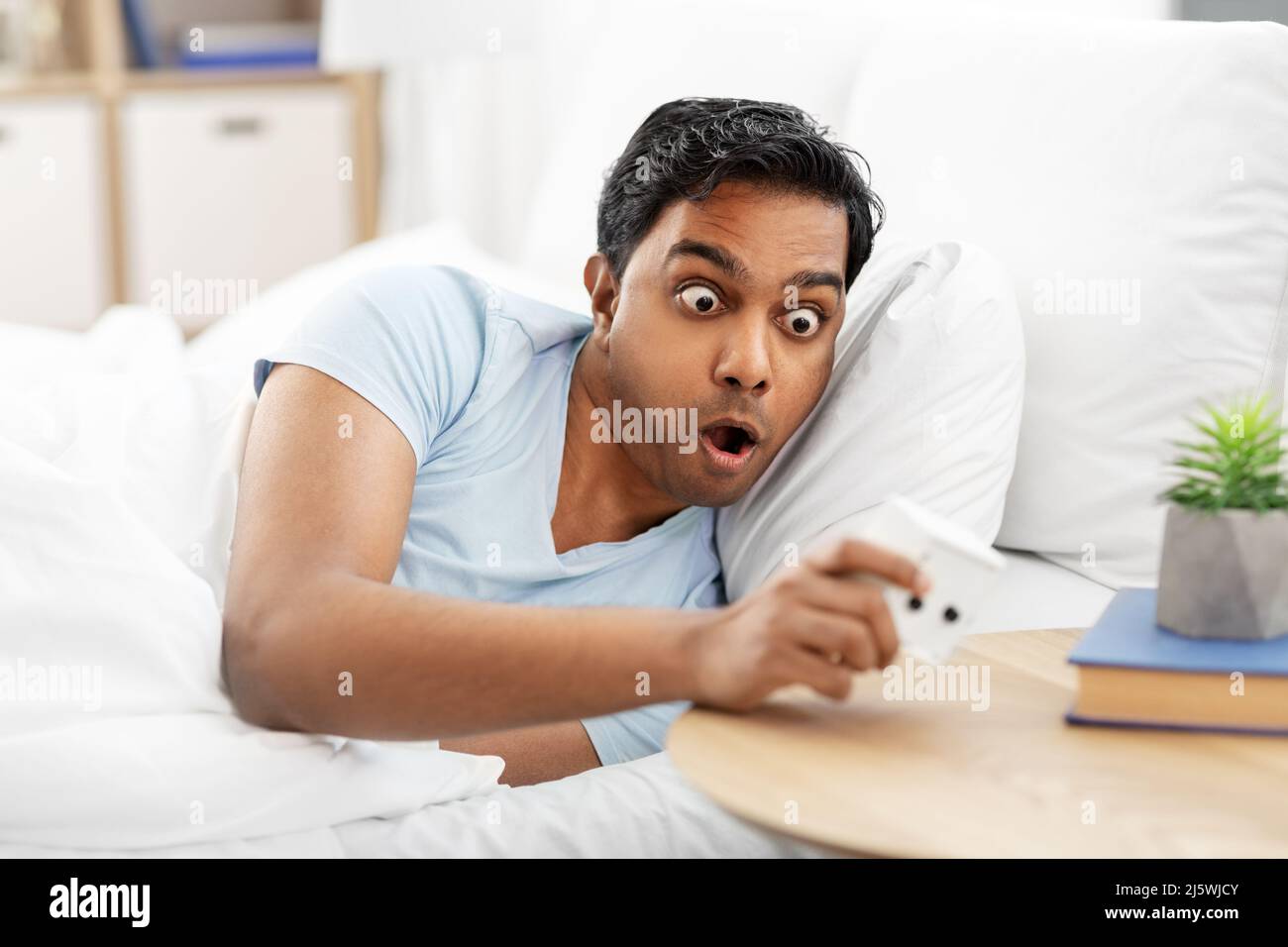 overslept indian man in bed looking at alarm clock Stock Photo - Alamy