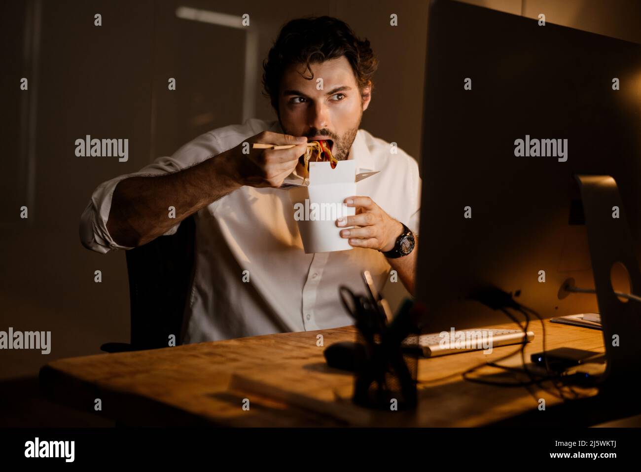 White man eating asian noodles while working with computer at office ...