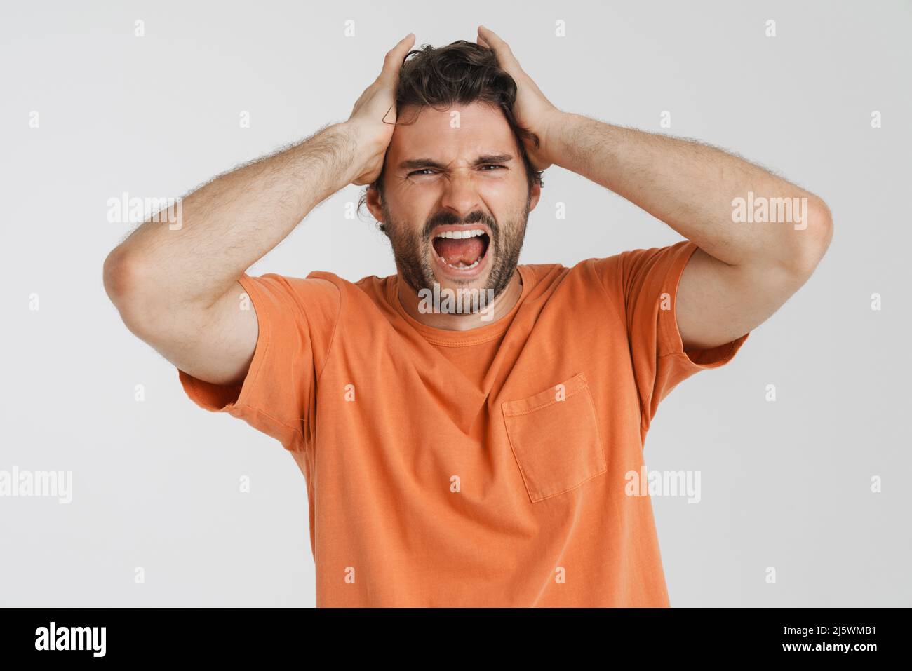 Young brunette man with bristle screaming while holding his head ...
