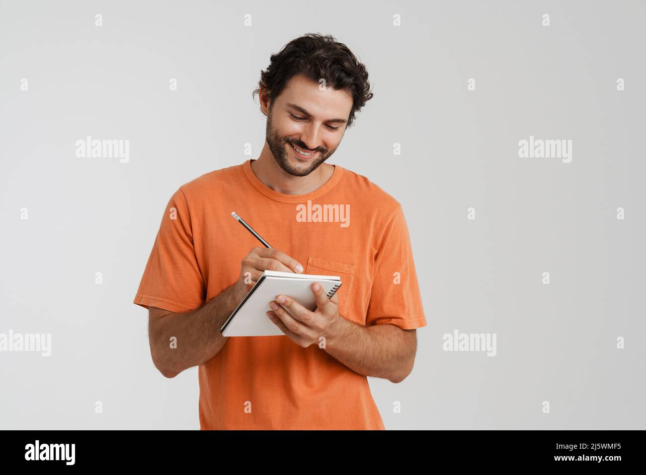 Young brunette man with bristle smiling while writing down notes ...