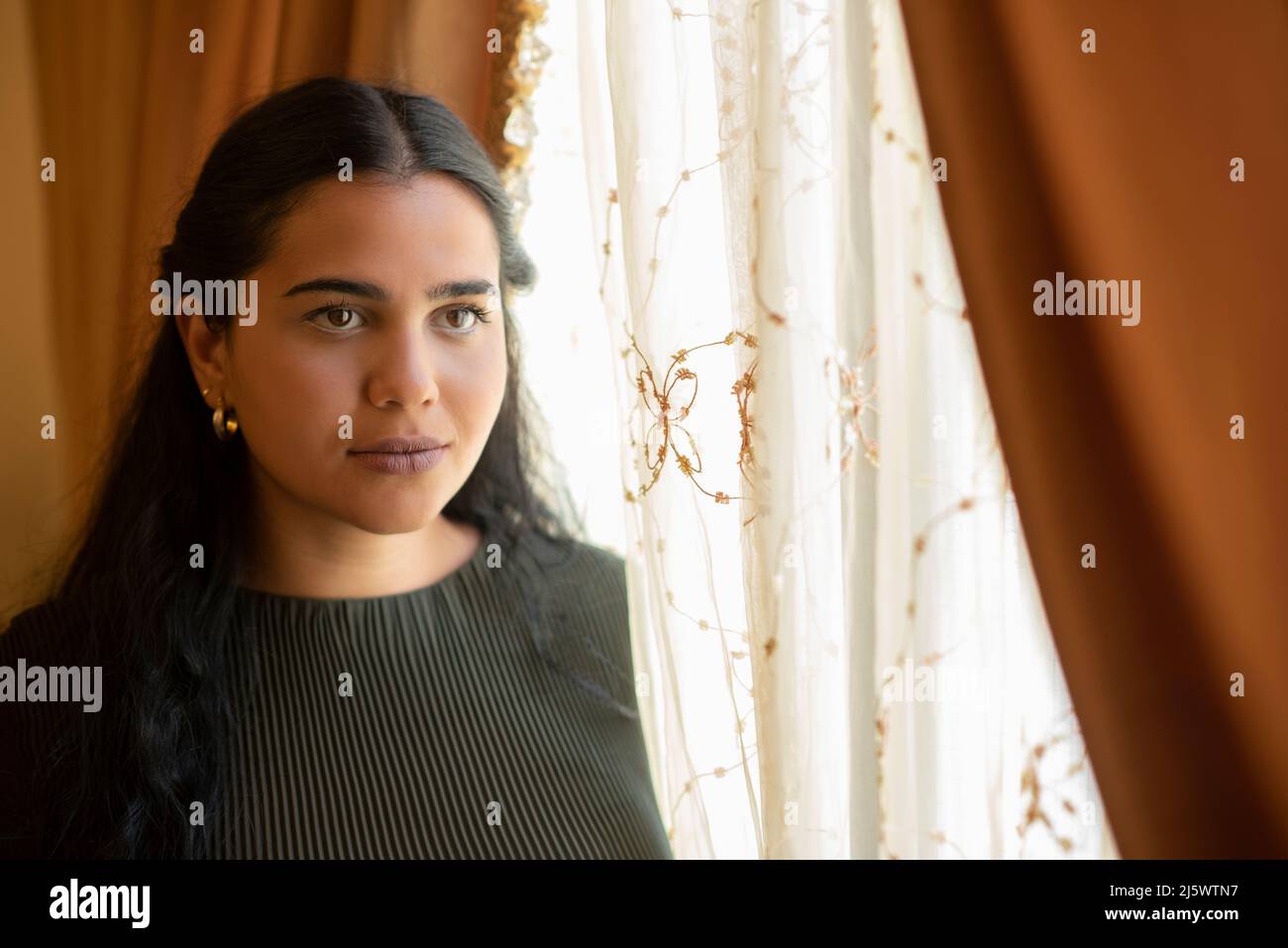 Serious woman by the window looking away Stock Photo - Alamy