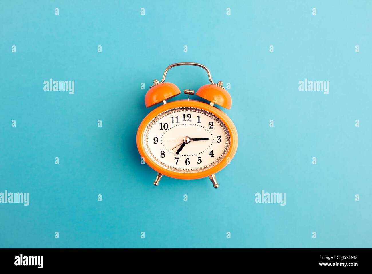 Vintage style orange alarm clock with bells on blue background with ...