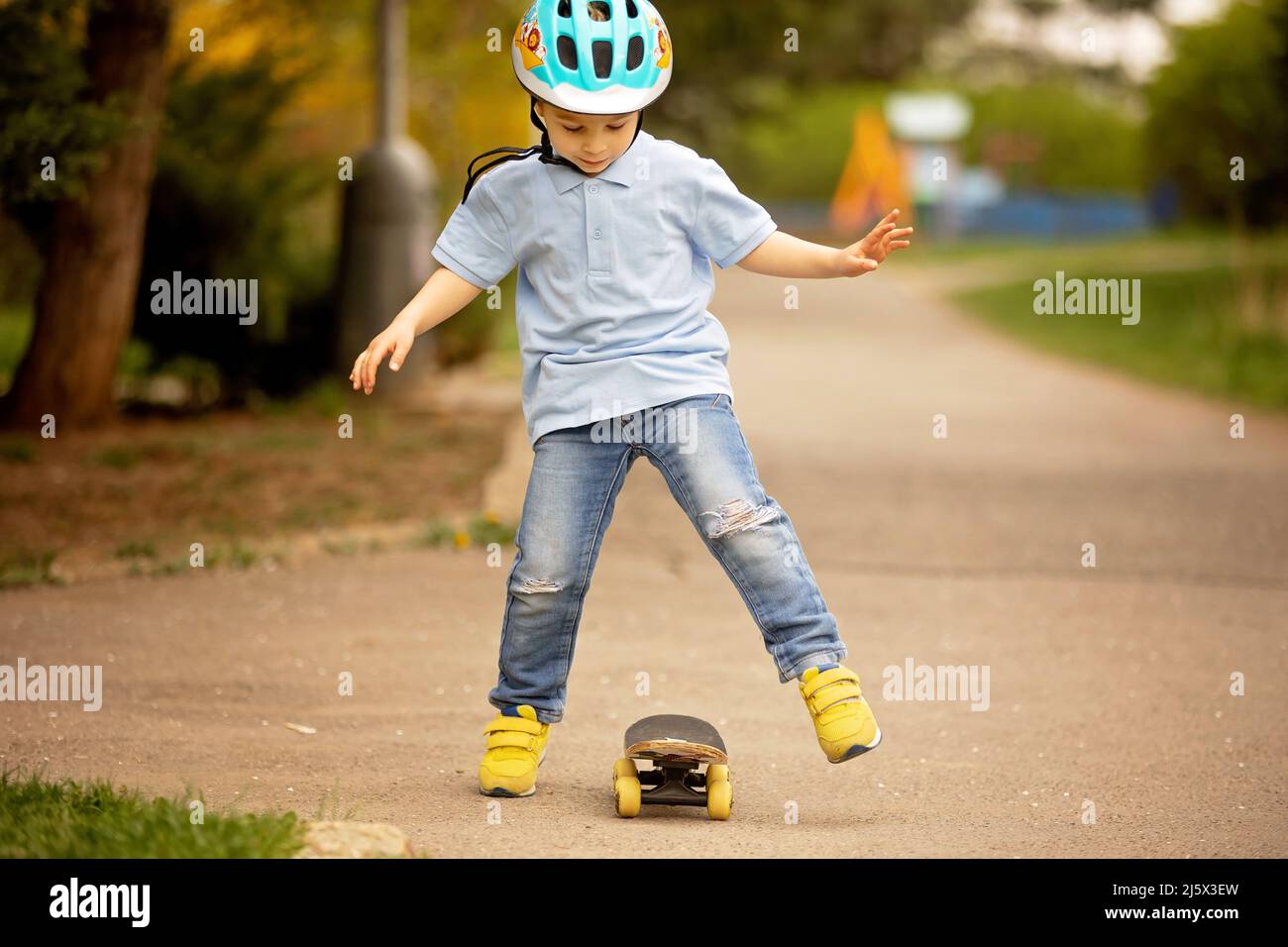 Little child, toddler boy, riding skateboard in the park for the first ...