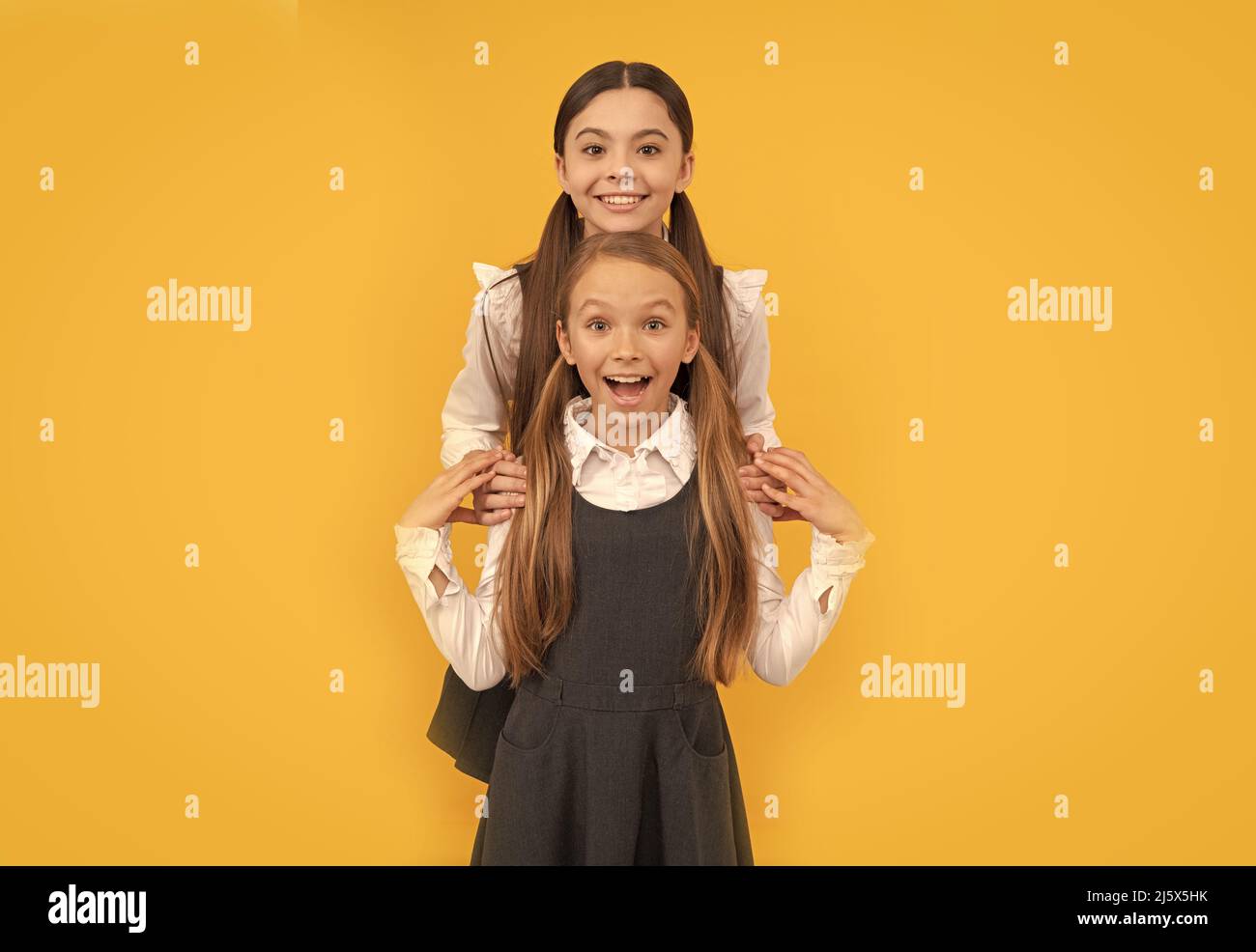 Happy school friends embrace in formal uniforms yellow background ...