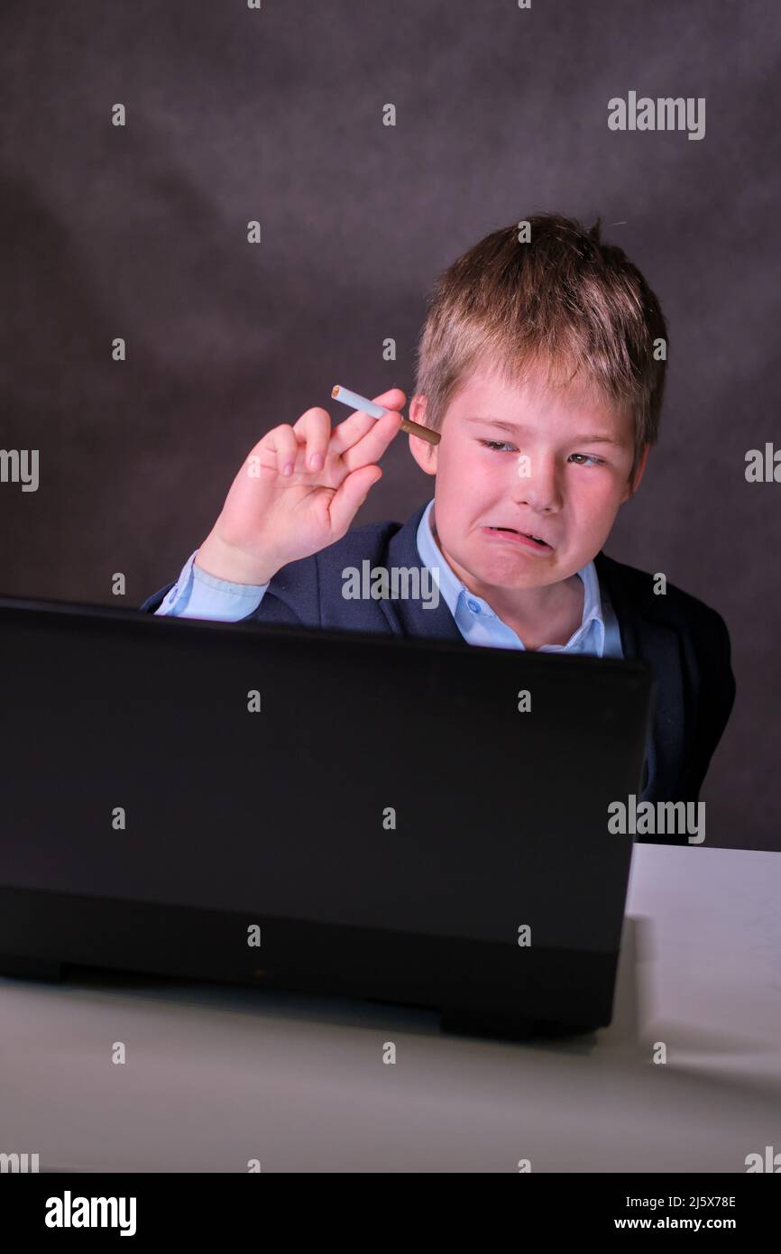 A boy in a school suit with a cigarette at the computer, copy space on ...