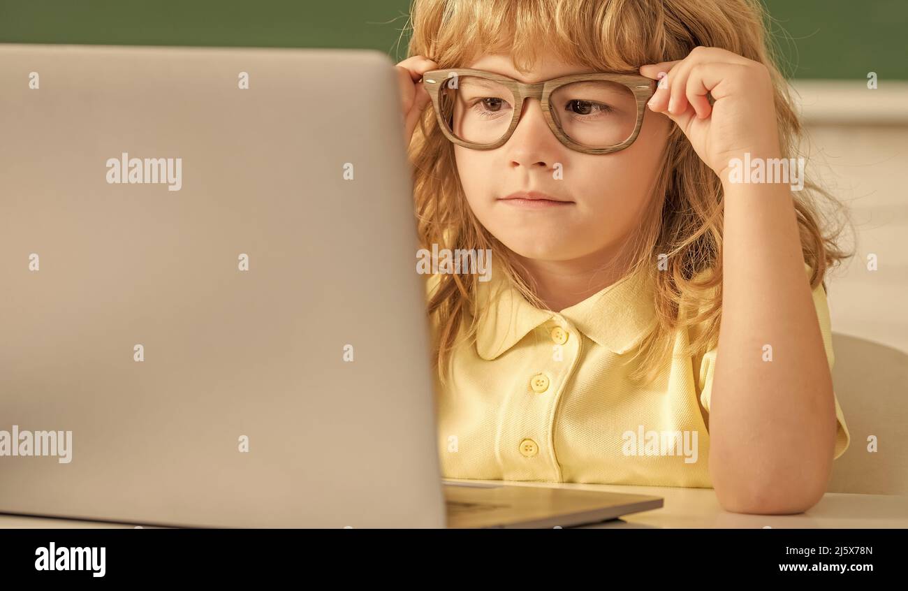 small kid boy in glasses study online in school classrrom with computer ...