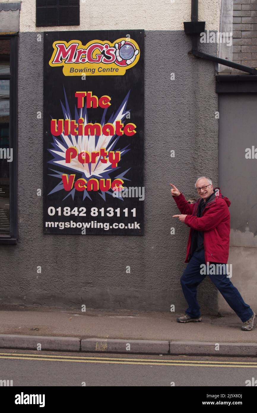 Man pointing excitedly at a bowling alley sign on the paevement outside ...