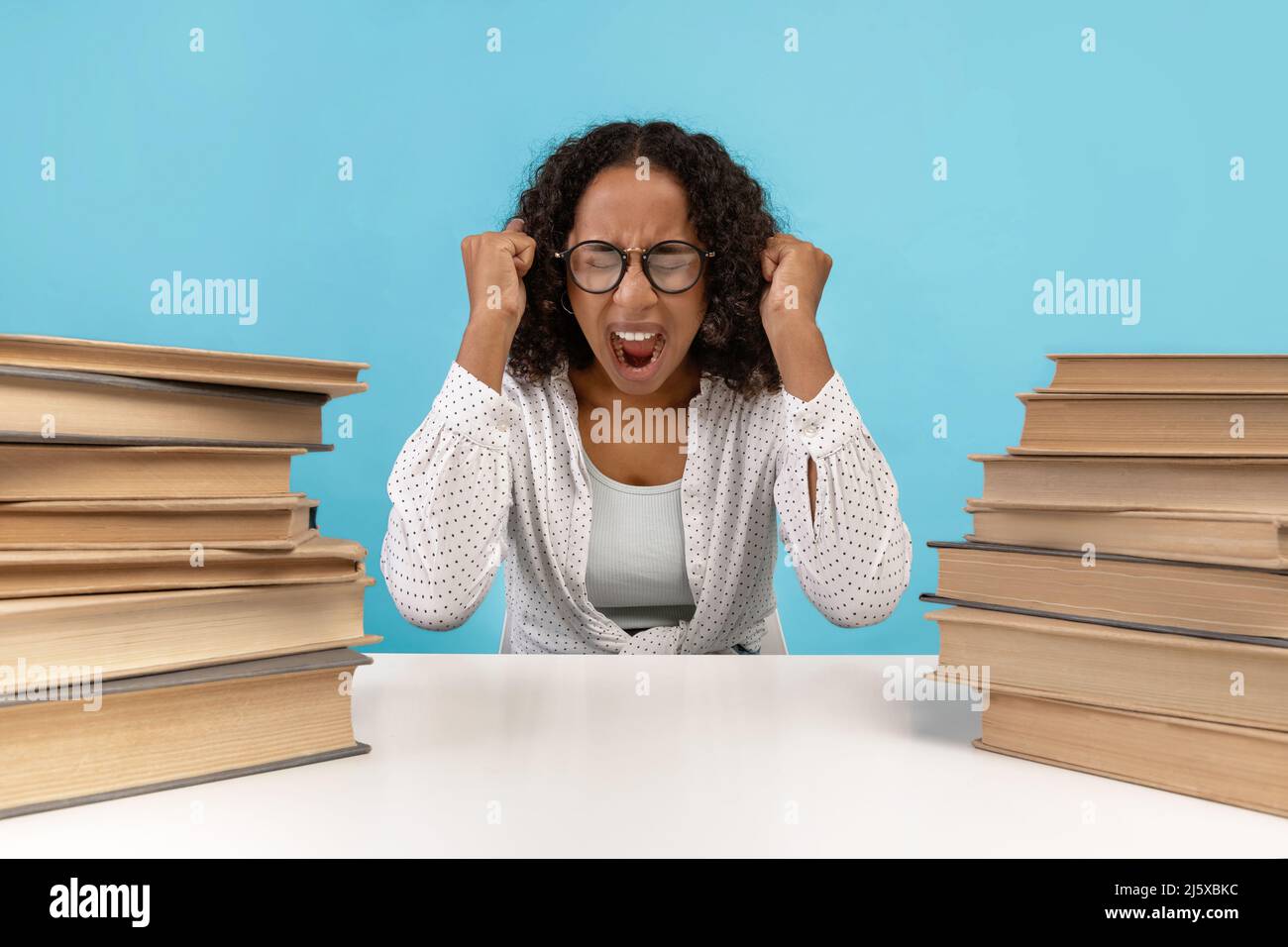 Desperate black female student with heaps of books sitting at desk ...