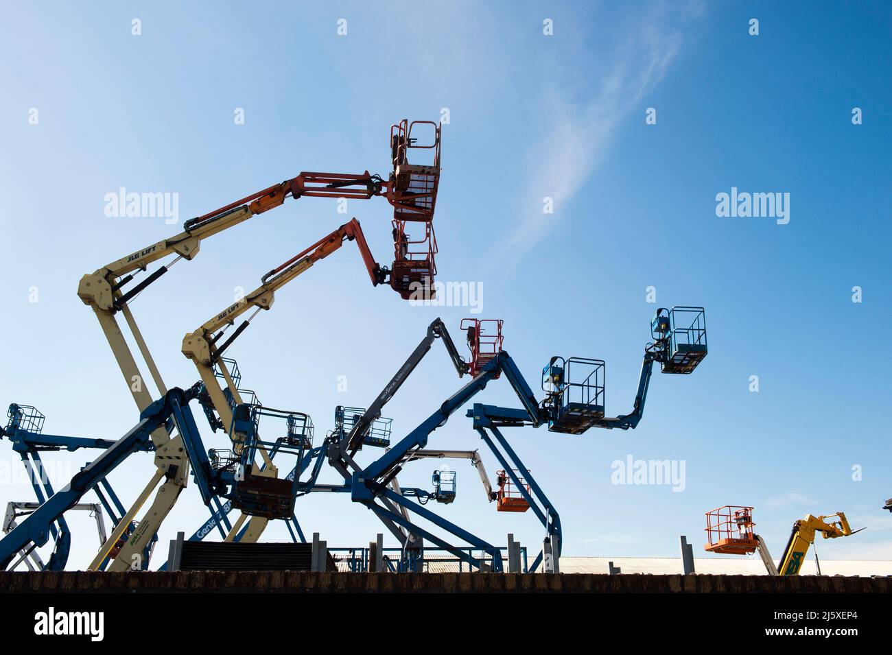 Cherry Pickers silhouetted agaianst a blue sky on an industrial estate ...