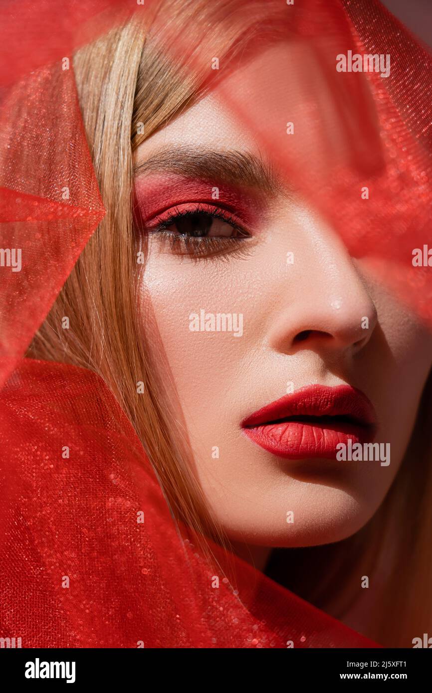 Model with red visage and obscure face looking at camera near cloth ...
