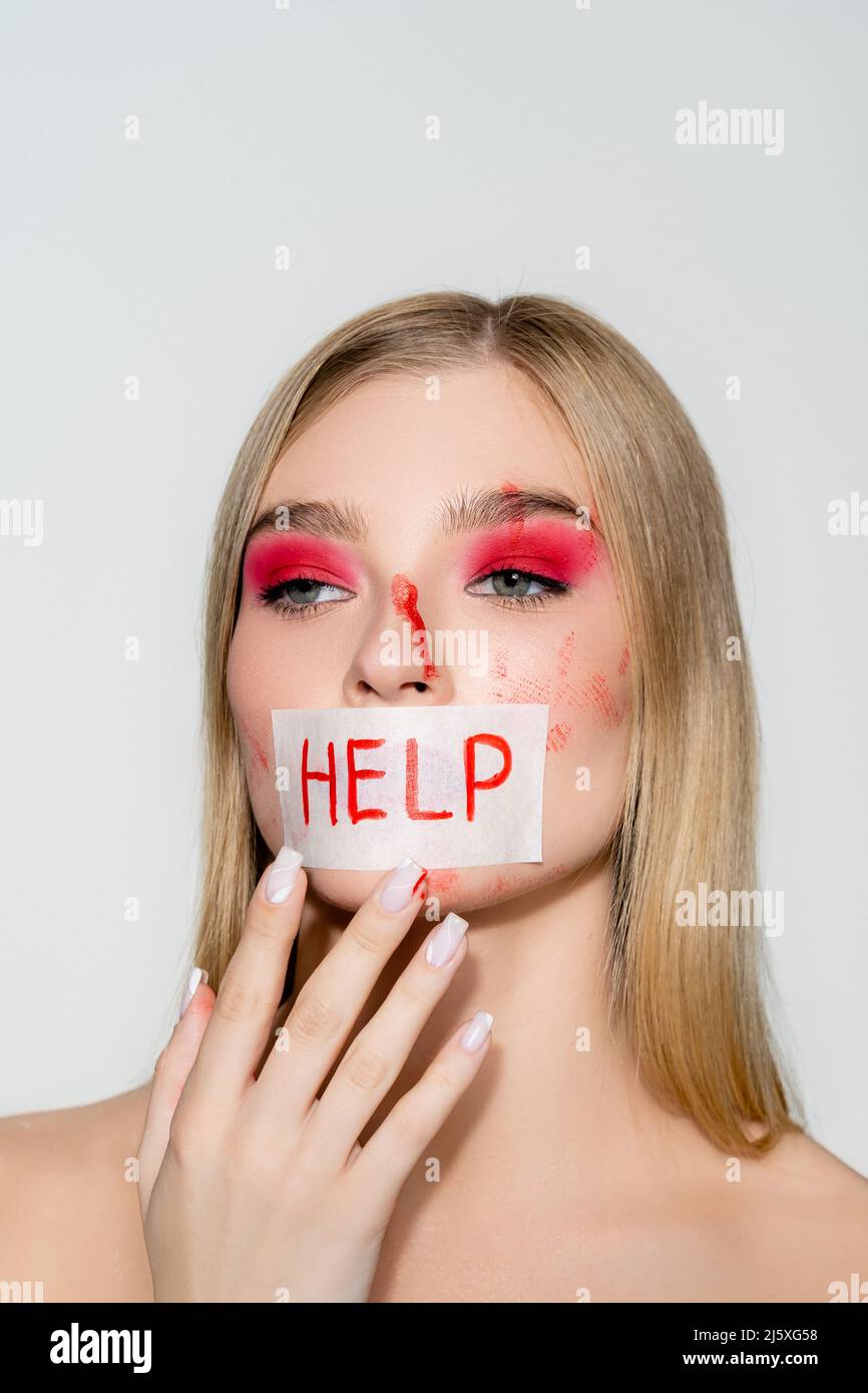 Young woman with blood on face and card with help lettering on lips ...