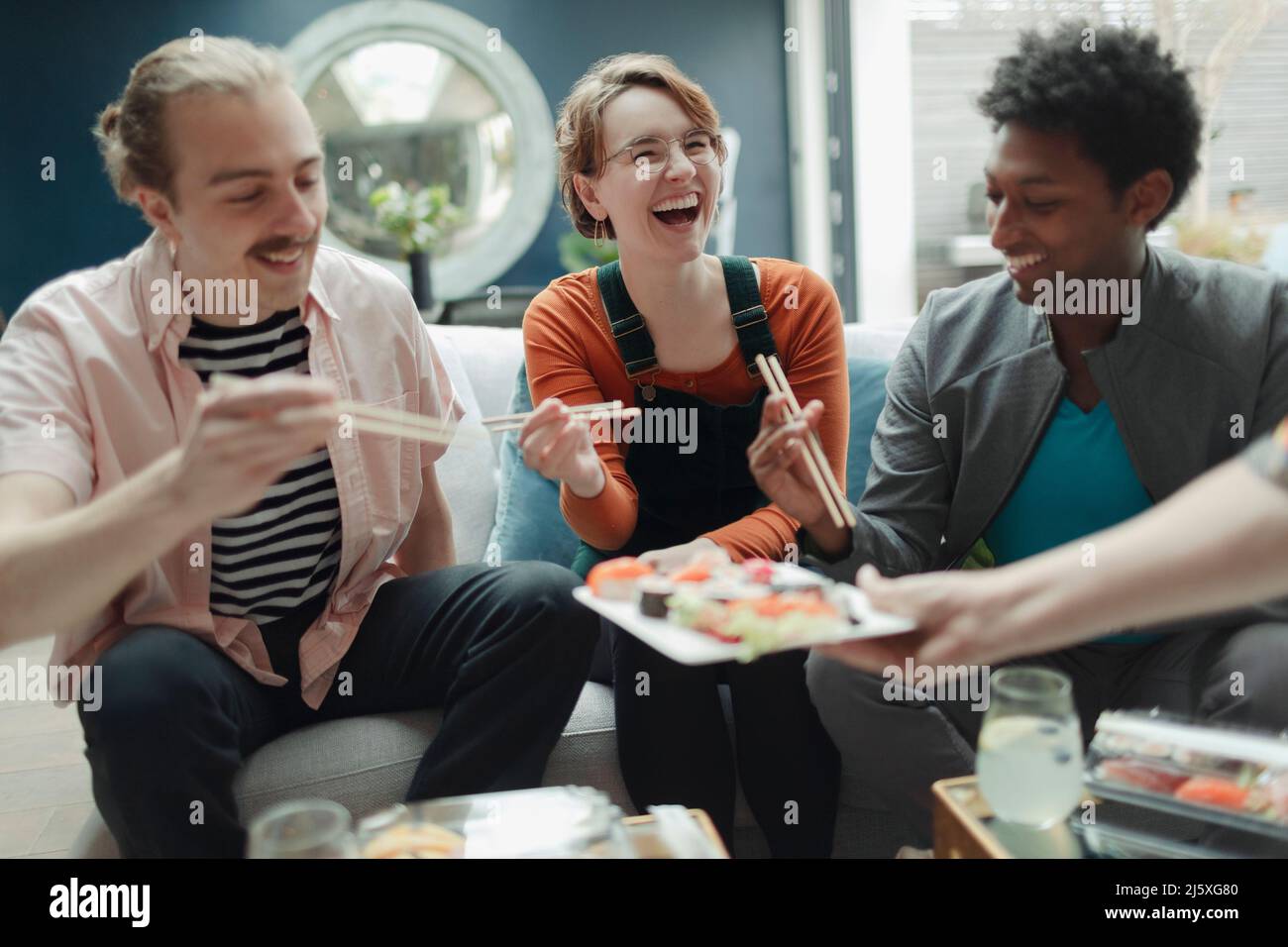 Happy friends sharing sushi in living room Stock Photo - Alamy