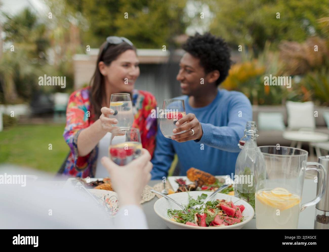 Happy couple toasting glasses with friend at patio table Stock Photo ...