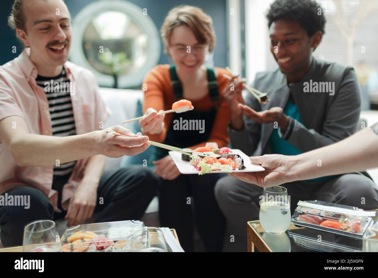 Happy friends sharing takeout sushi in living room Stock Photo - Alamy